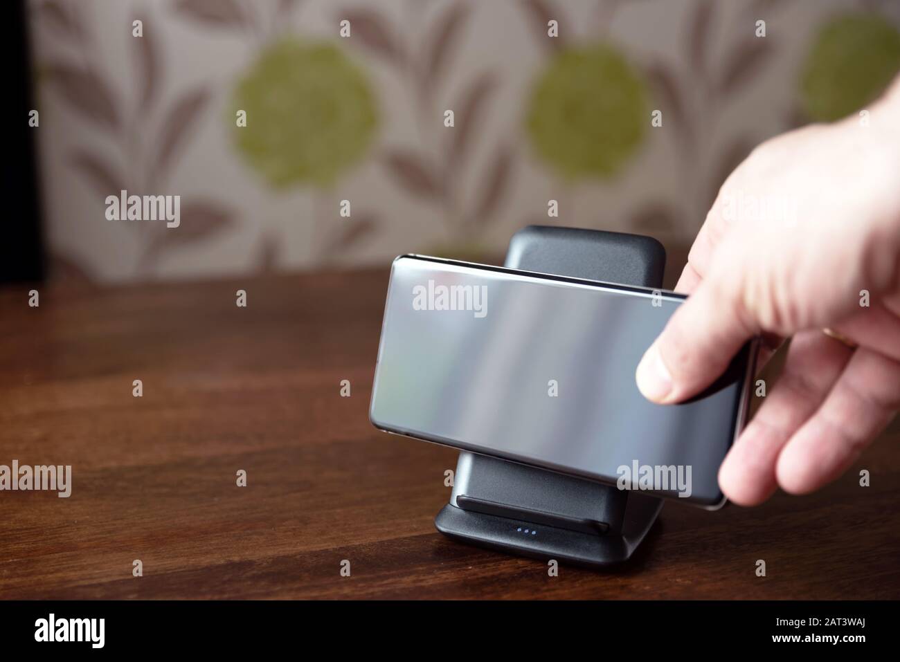 smartphone wireless charging on charging stand on wooden table. male ...