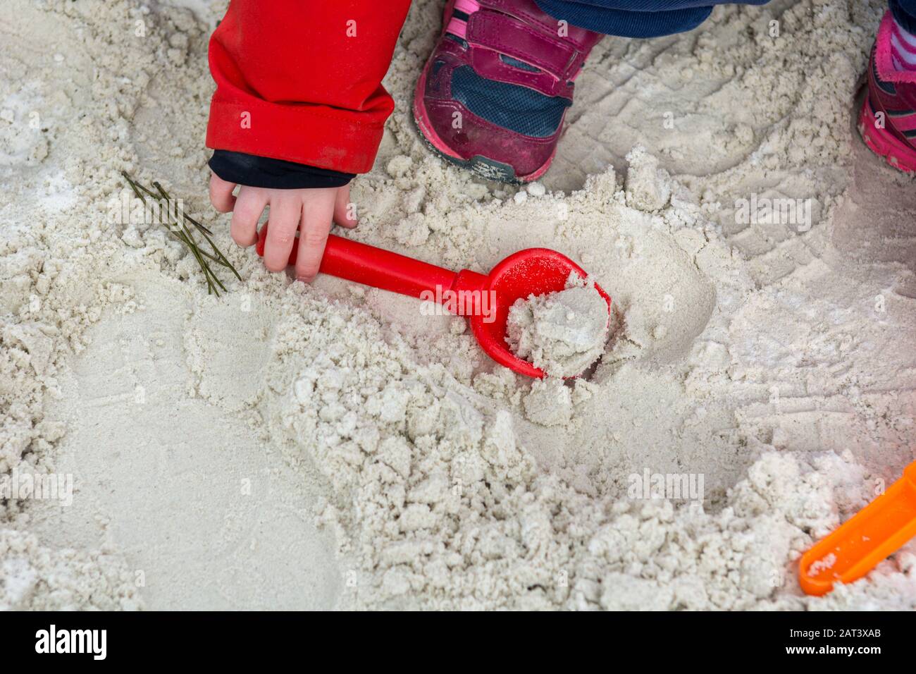 Drop down view of child holding a red plastic shovel in sand box ...