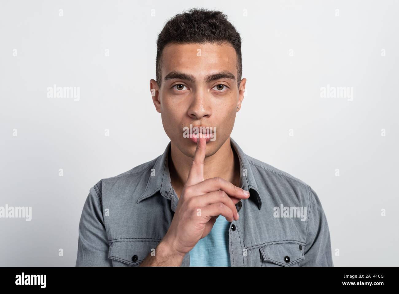 Man saying hush be quiet with finger on lips gesture on white wall ...