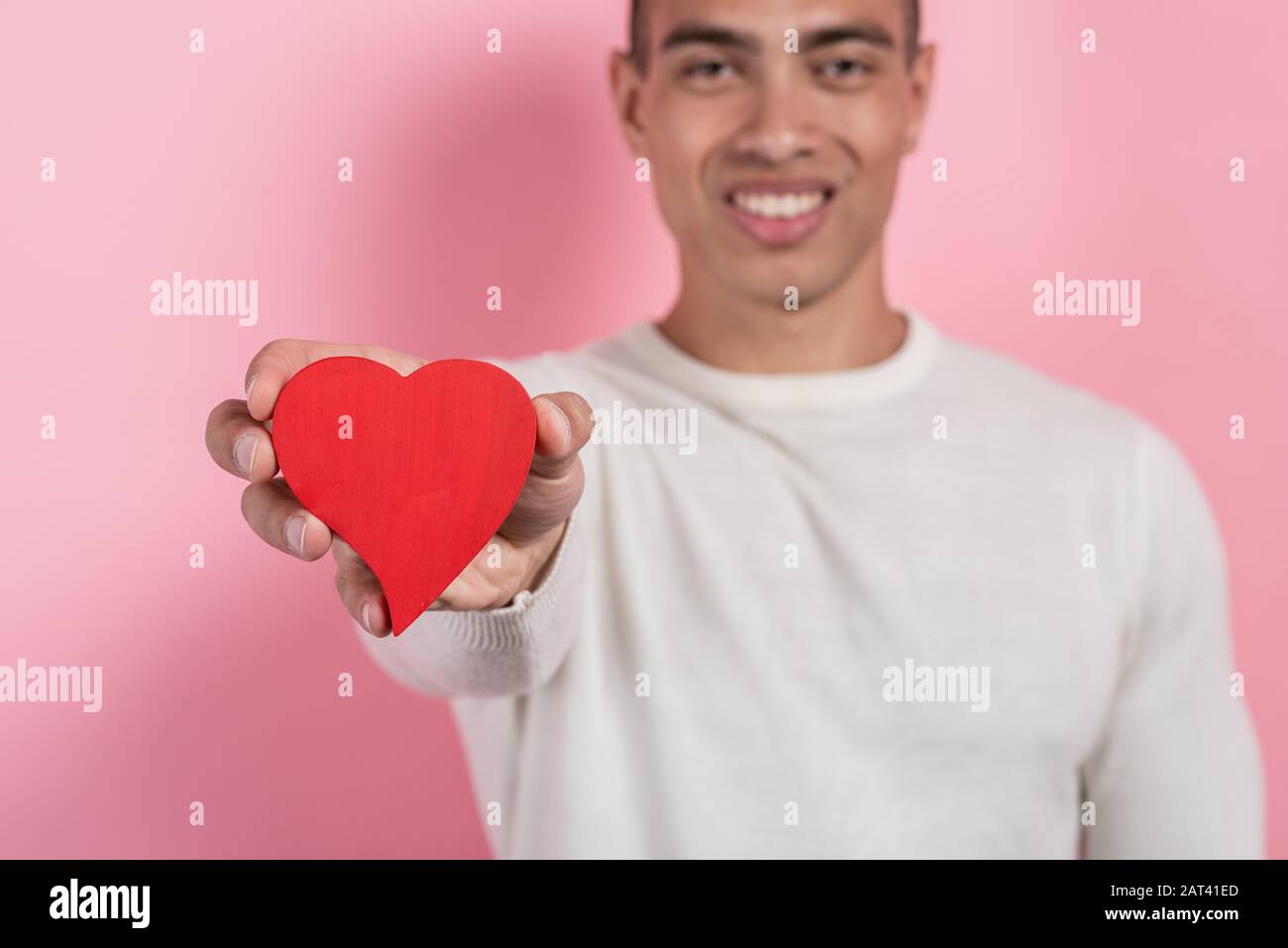 Mulatto man holding a heart-object in his straight hand. Focus to a ...
