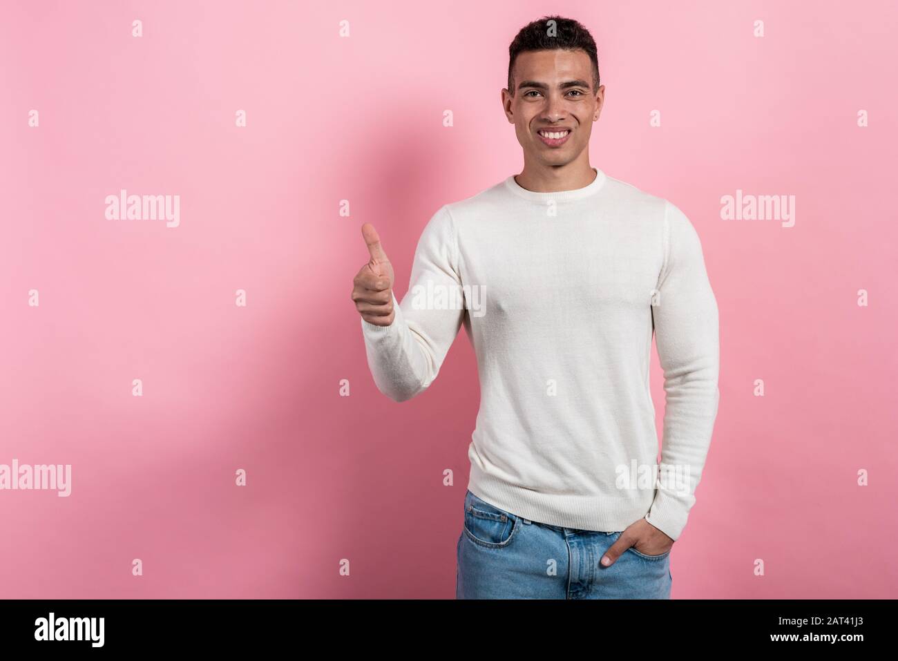 Pretty mulatto man on pink studio background shows thumb up. Male half ...