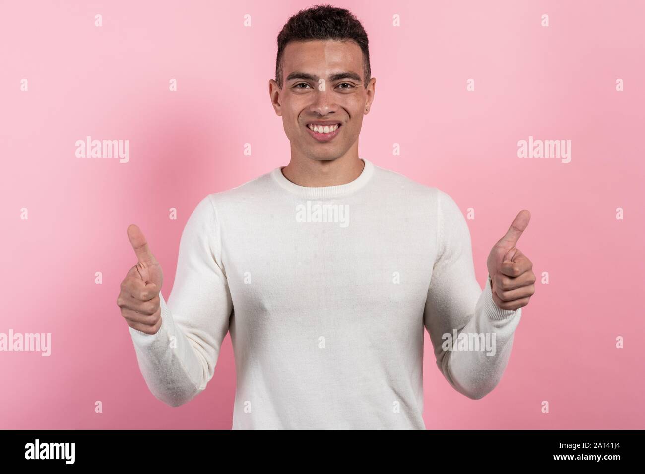 Happy mulatto man on pink studio background shows two thumb up. Gesture ...