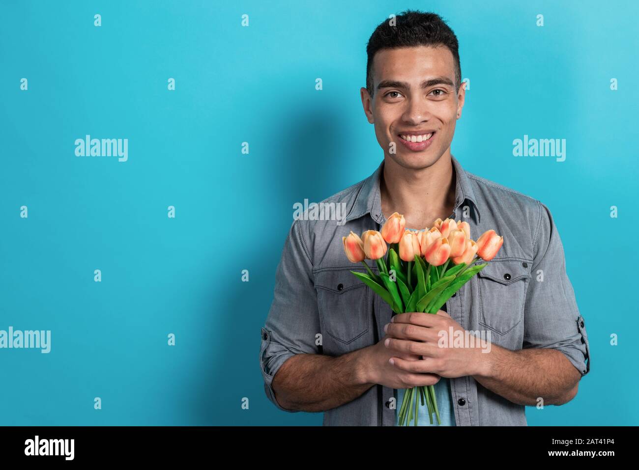 Portrait of happy mulatto man standing against a blue wall holding a ...