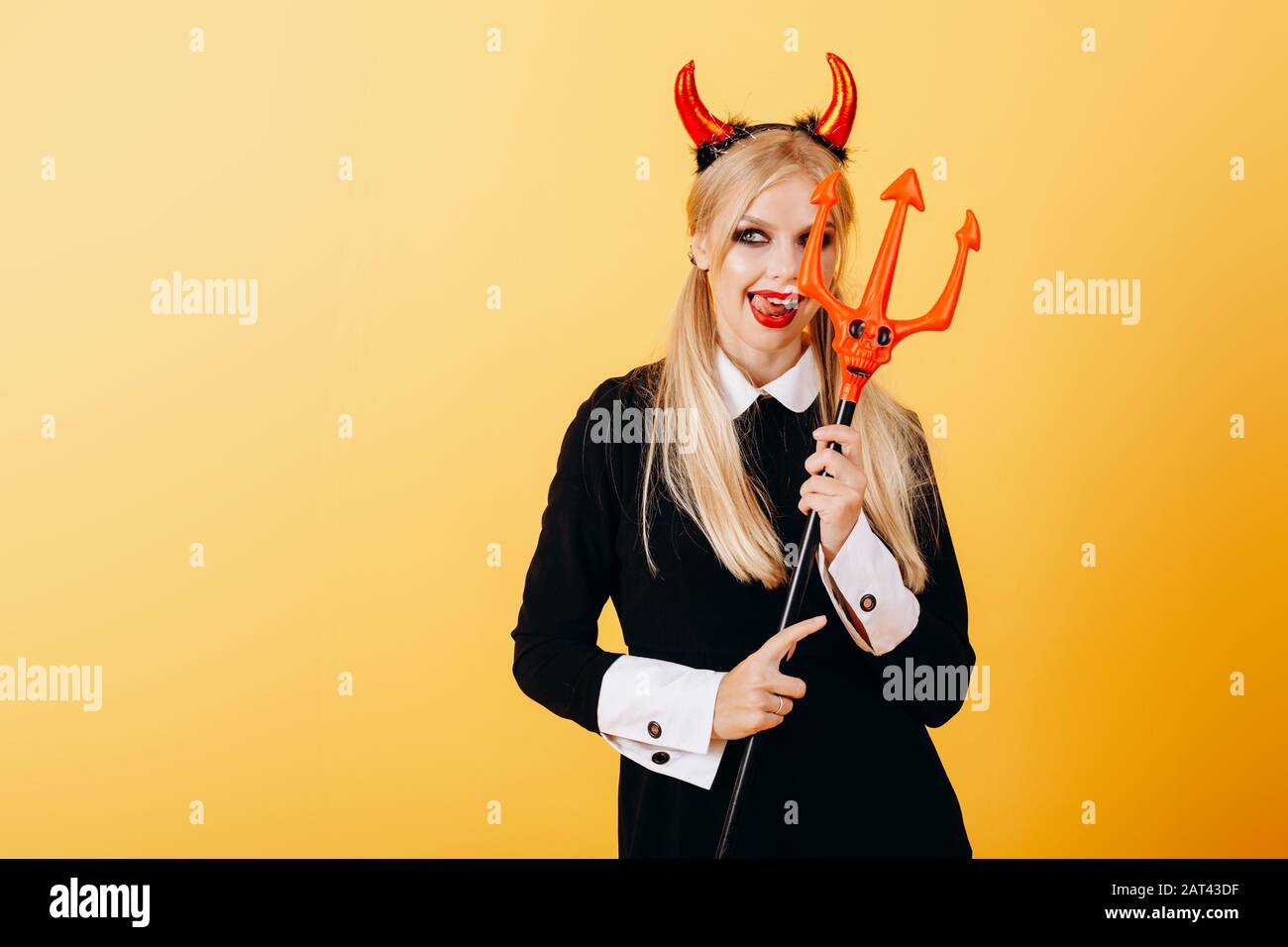 devil woman standing against a yellow background and showing the tongue ...