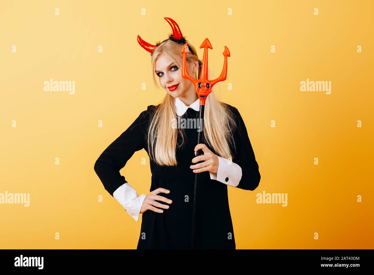 devil woman standing against a yellow background and playfully looking ...