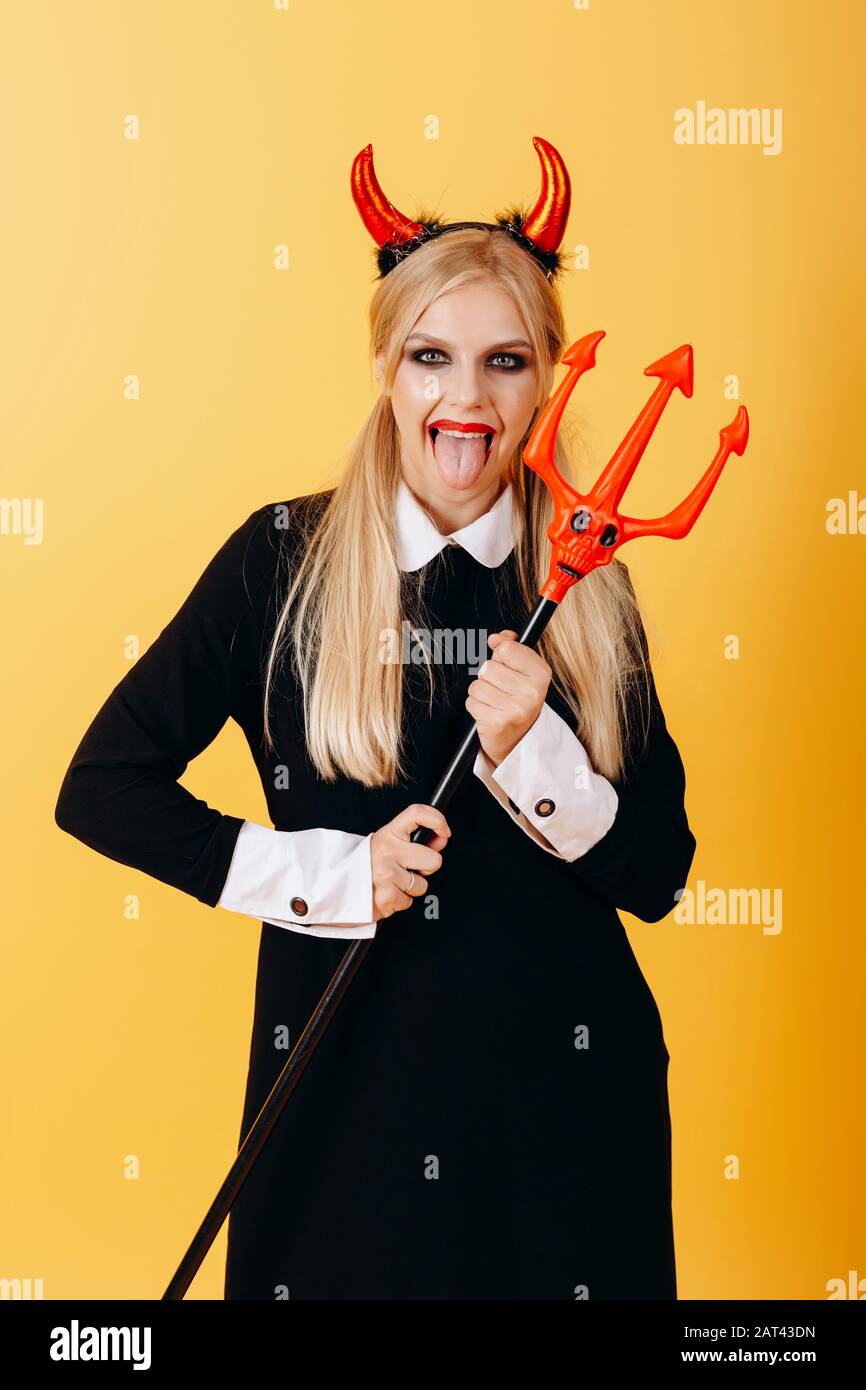 devil woman standing against a yellow background and showing the tongue ...