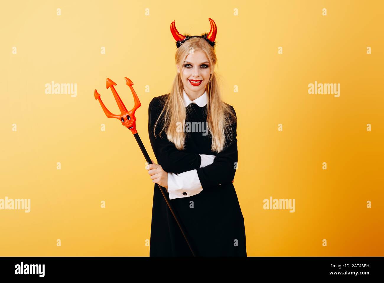 devil woman standing against a yellow background Stock Photo - Alamy