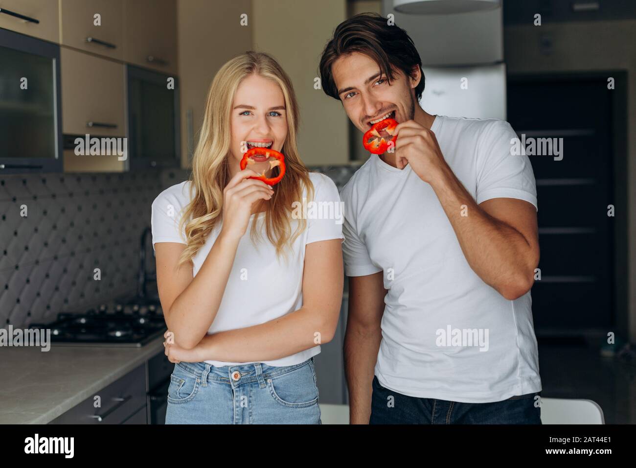 Happy couple in the kitchen standing with healthy food and eating a ...