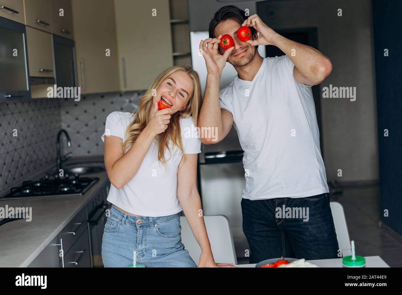 Couple in the kitchen standing with healthy food and hane a funny time ...