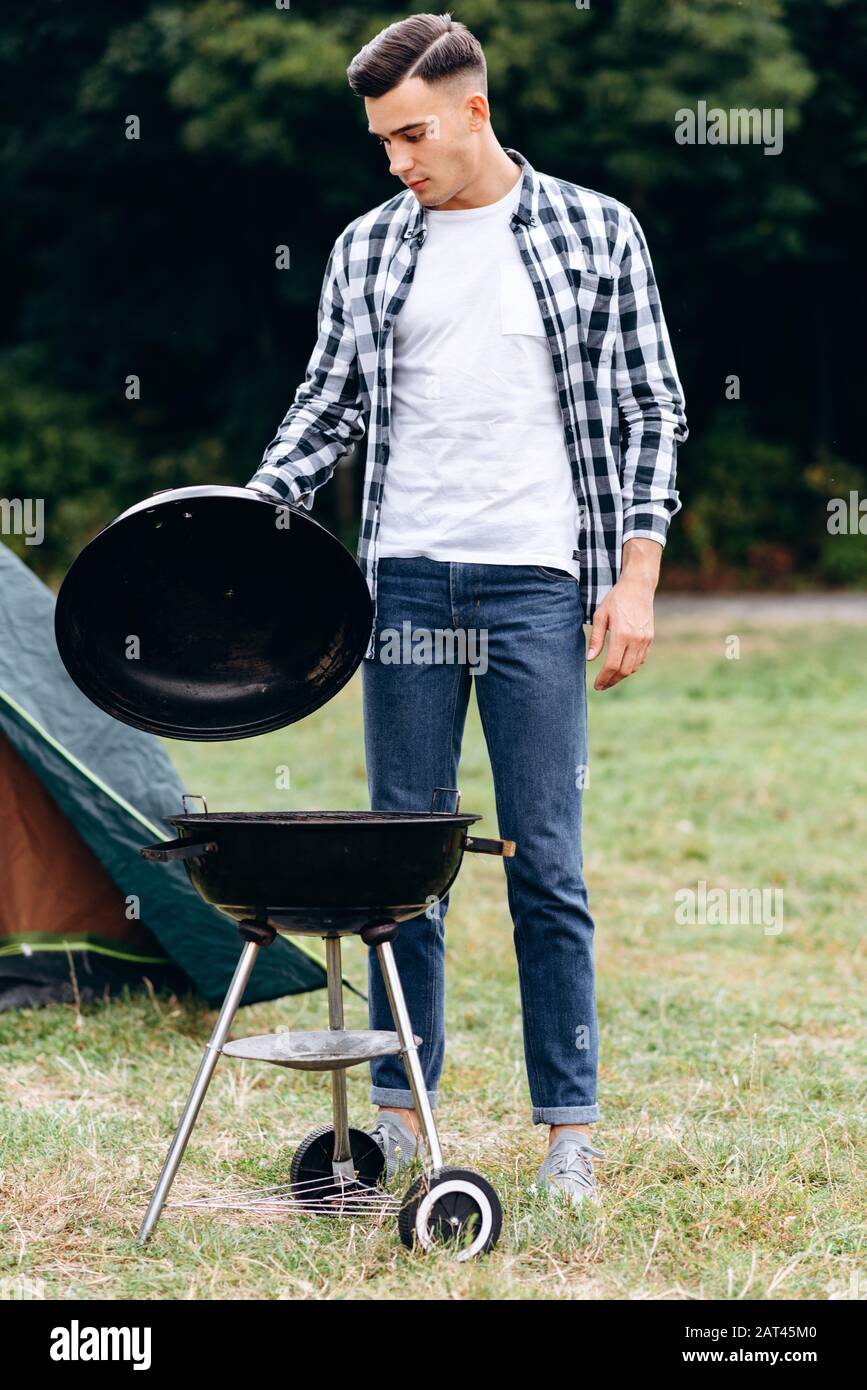 Young guy cooking in the camping/ Standing and opens the lid of the ...