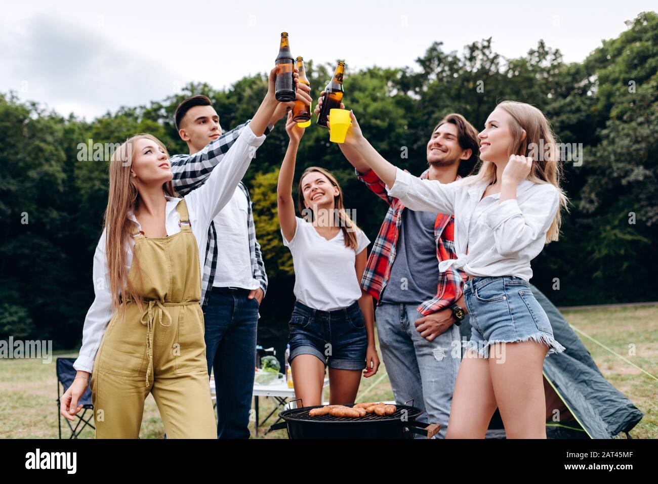 A company of friends raising a bottles with a beer in the camping ...