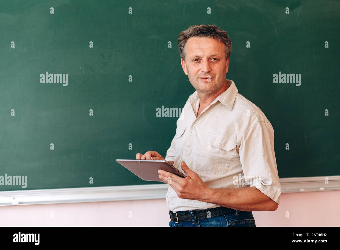 Middle age teacher next the blackboard holding an ipad and explain a ...