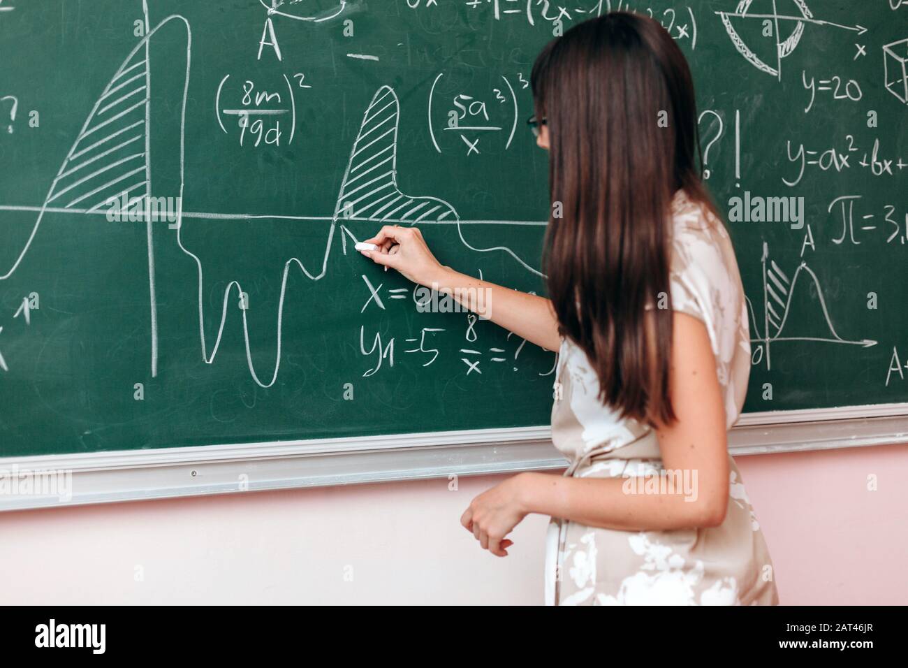 Teacher write an example on the blackboard and explain a lesson.- Image ...