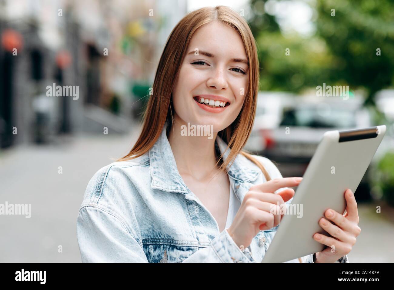 Closeup portrait of young woman holding an ipad and standing outdoor ...