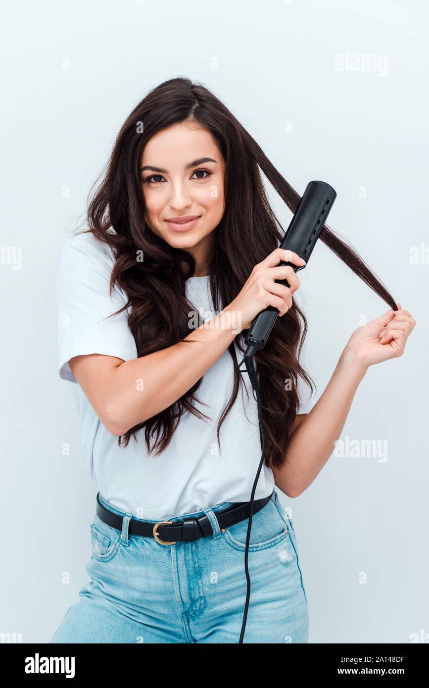 Smiling young woman straightening her hair with a straightener on the ...