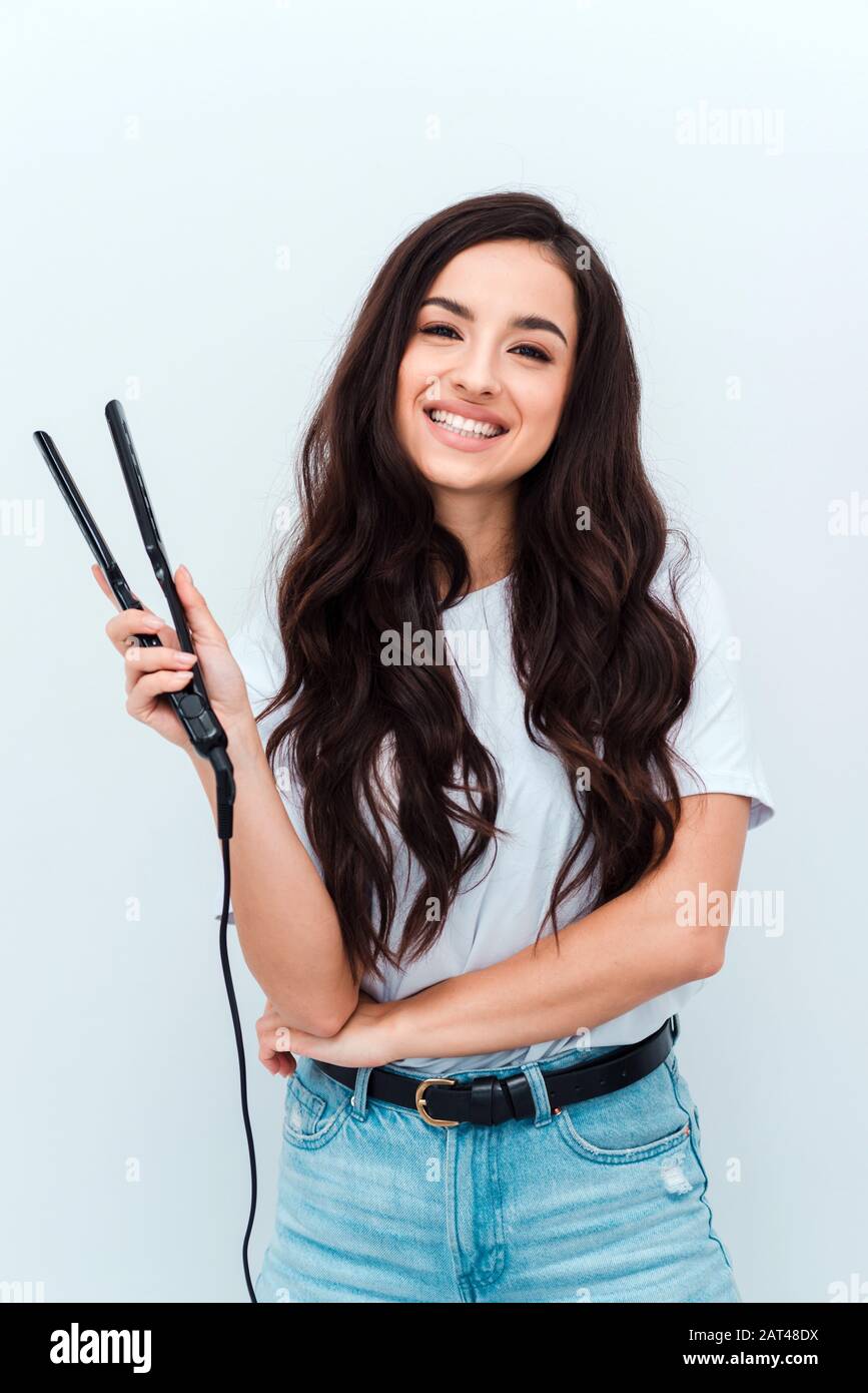 Portrait of pretty cute girl using a straightener for her curly hair ...