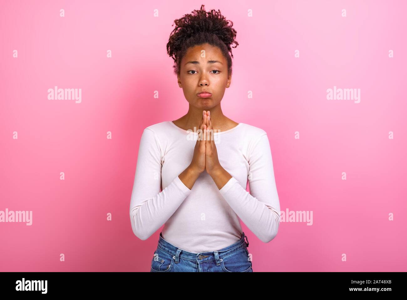 Studio shot of woman in supplication pose over pink background looking ...