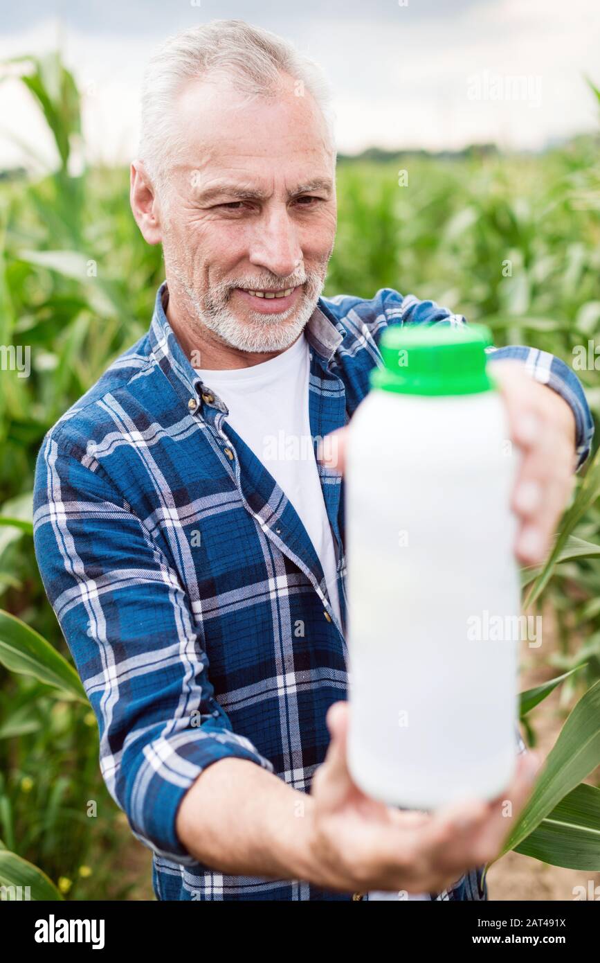 Middle aged farmer standing in a field looking on a bottle with ...