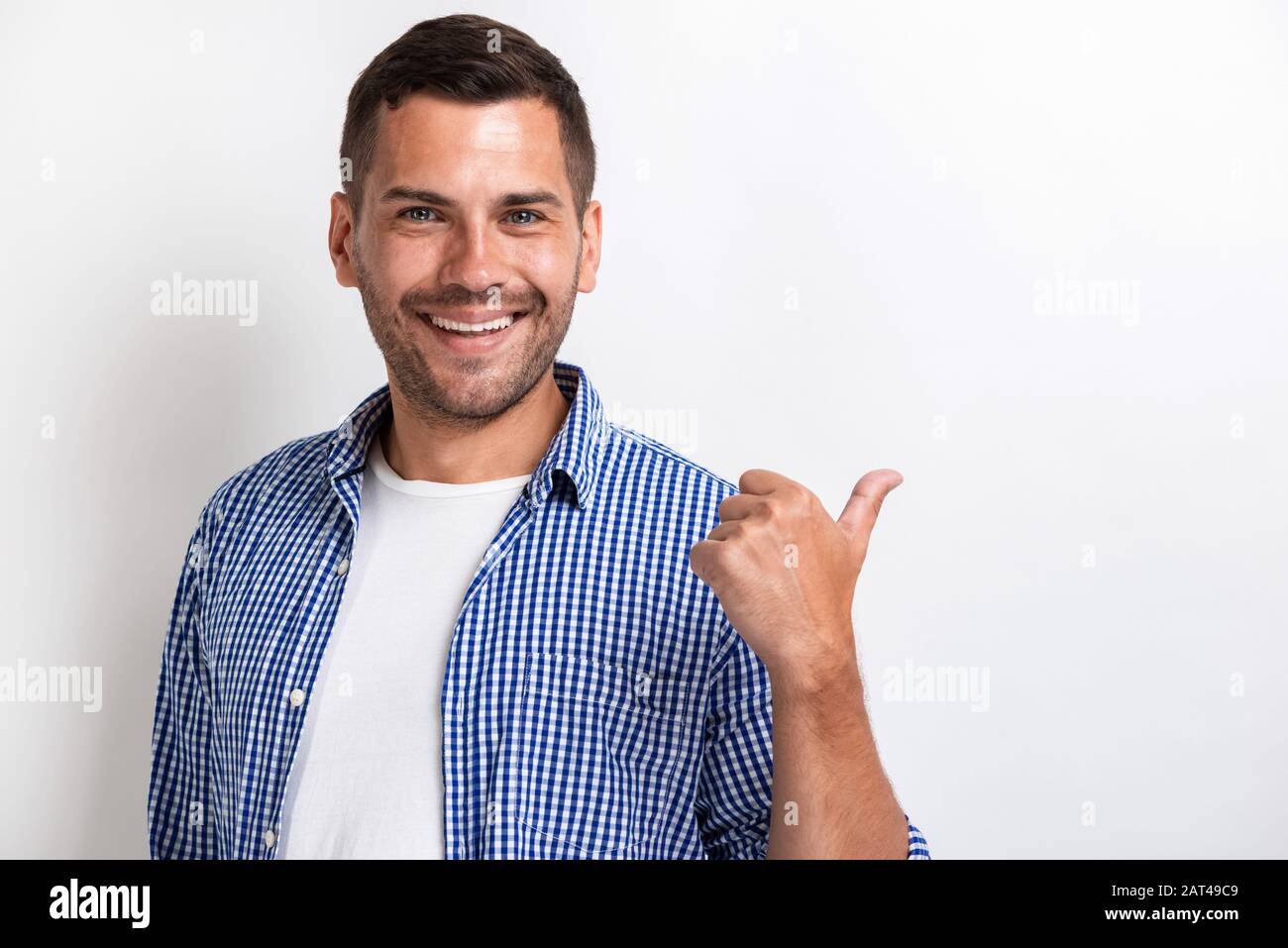 Handsome happy man pointing by his big finger backward and looking at ...