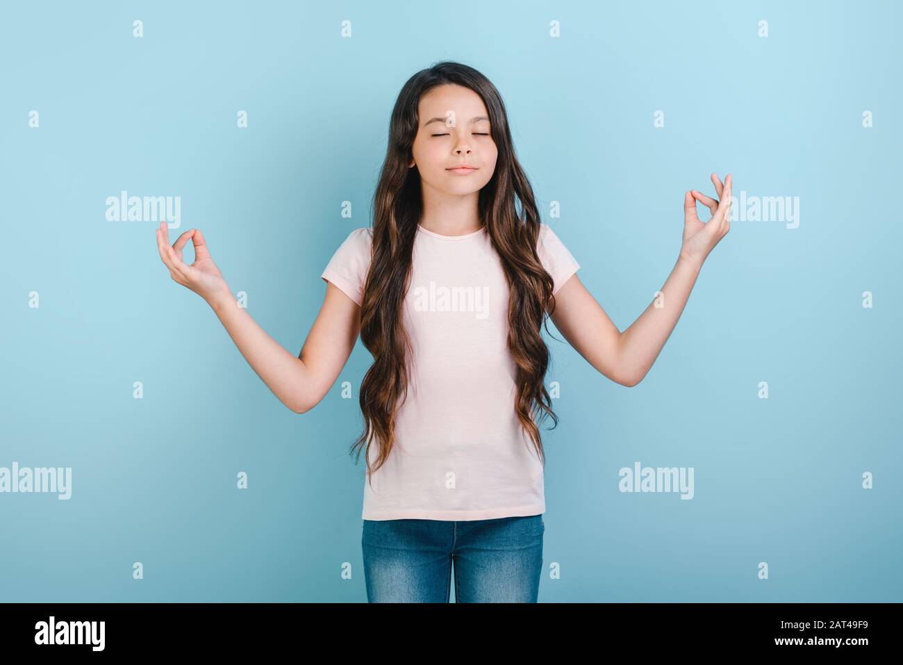 Girl standing in meditation pose over blue studio background. - Image ...