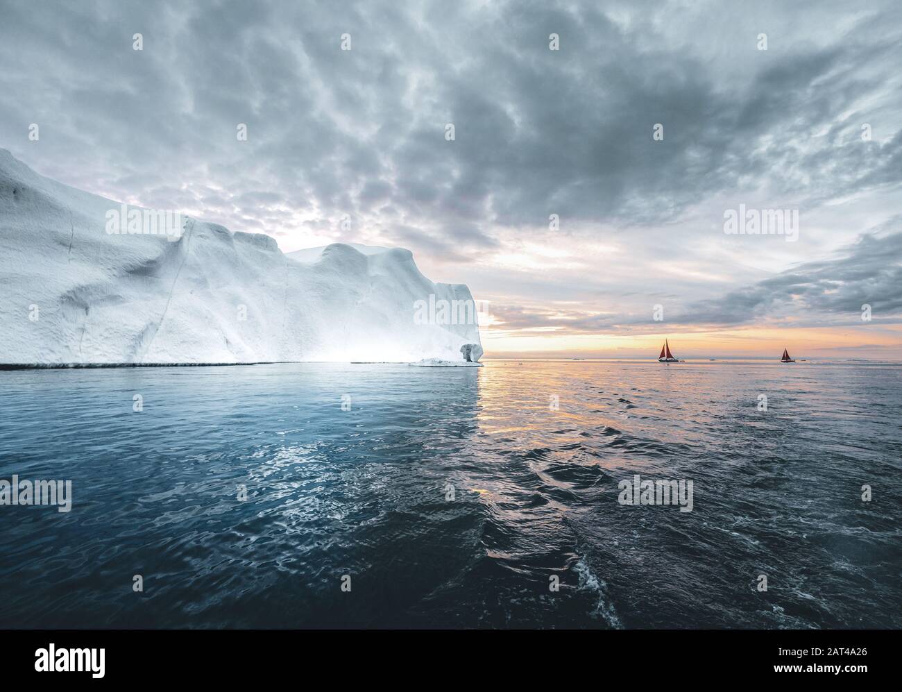 Beautiful red sailboat in the arctic next to a massive iceberg showing ...