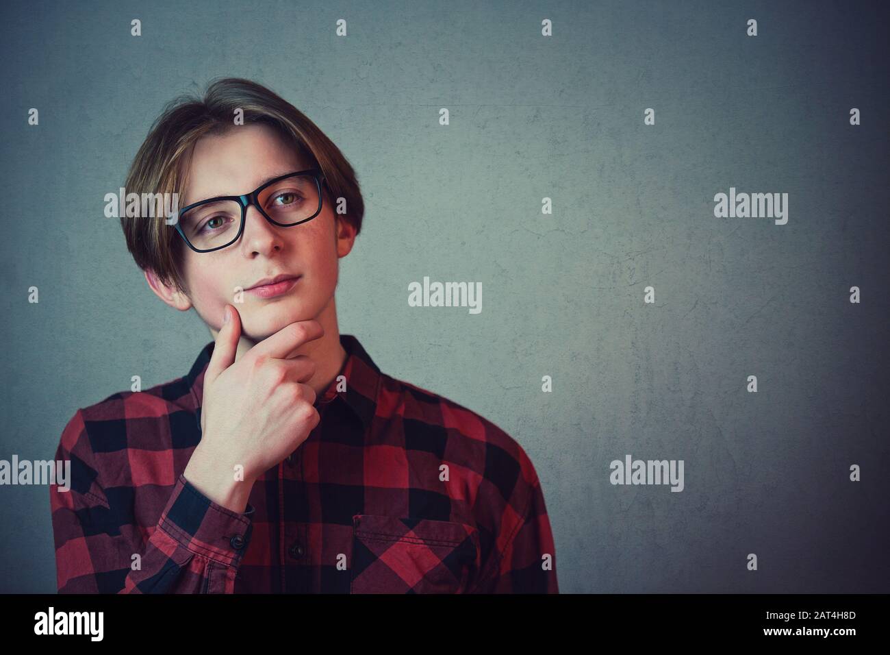 Teenage boy confident thinking, keeps one hand under chinlooking away ...