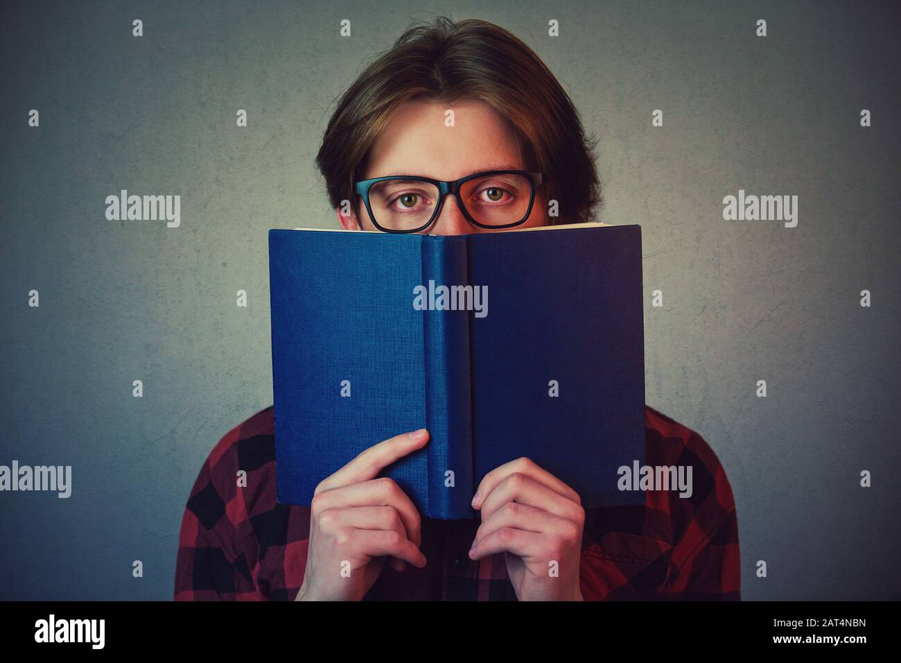 Close up portrait student boy hiding behind a opened blue book isolated ...
