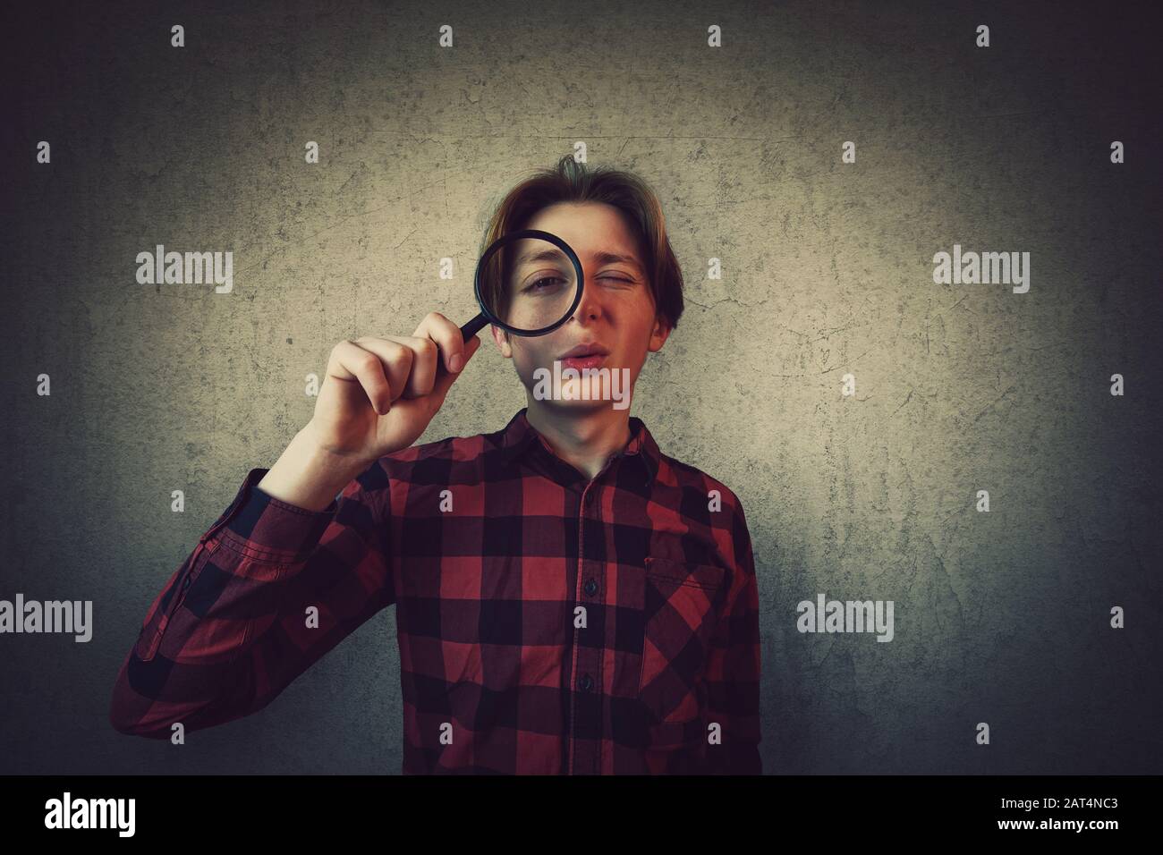 Curious young man looking through the magnifying glass isolated on grey ...