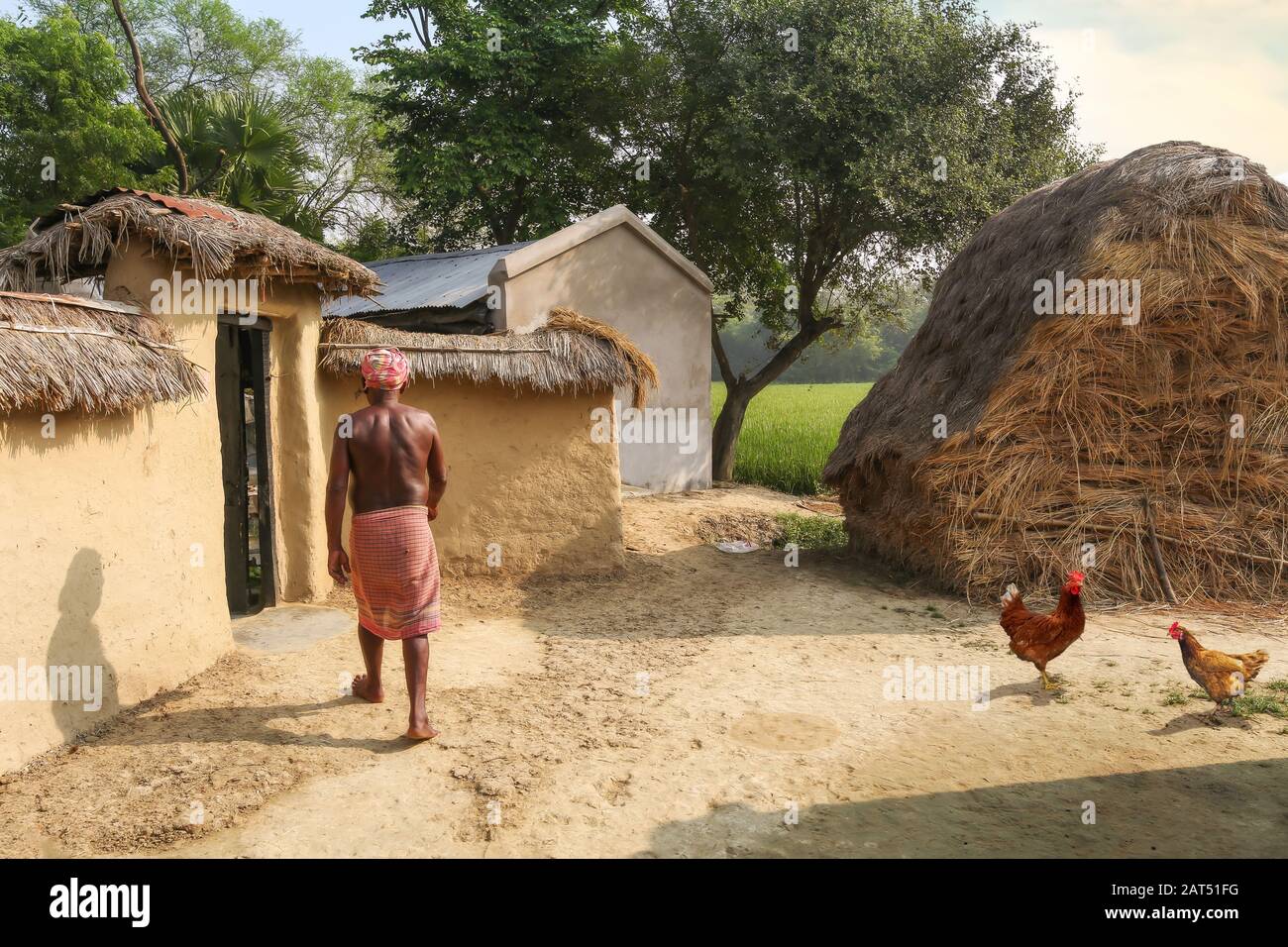 Rural man near his mud hut with view of haystack at an Indian village ...