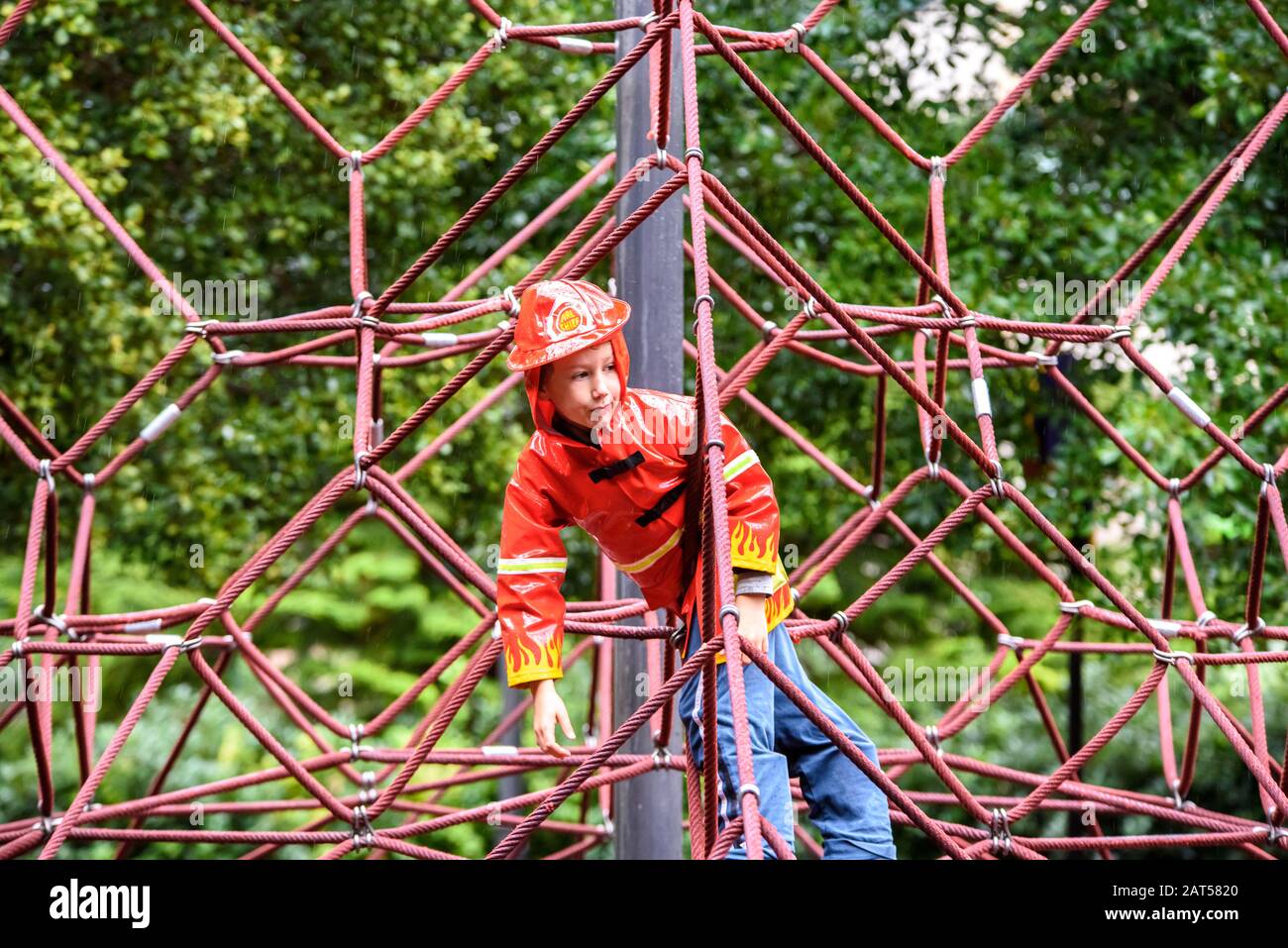 Child with red raincoat of firefighter clings to a rope in a playground ...