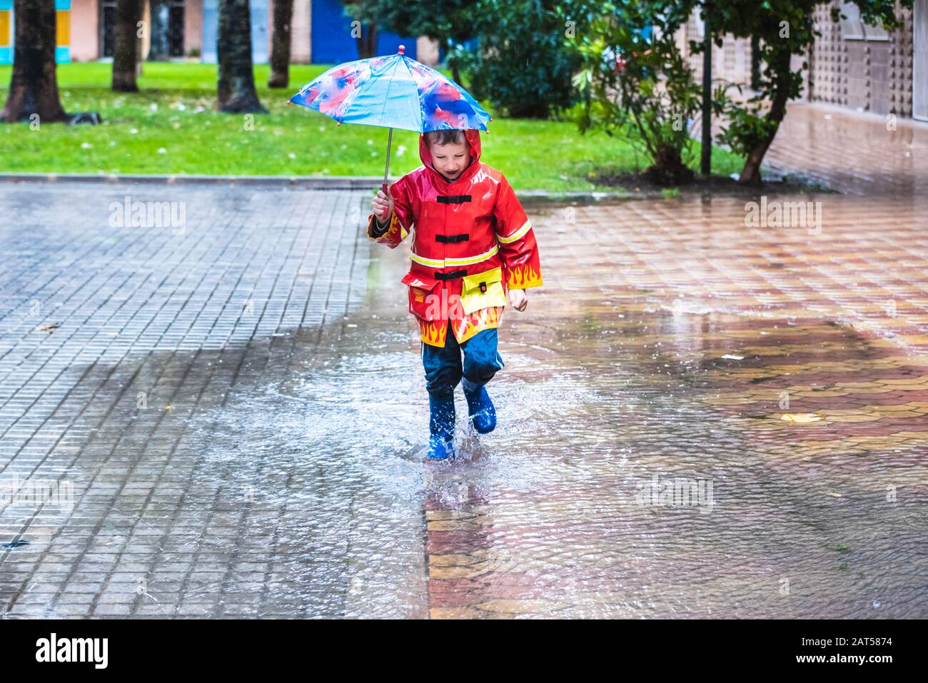 Boy with red raincoat disguised with umbrella splashes in a puddle of ...