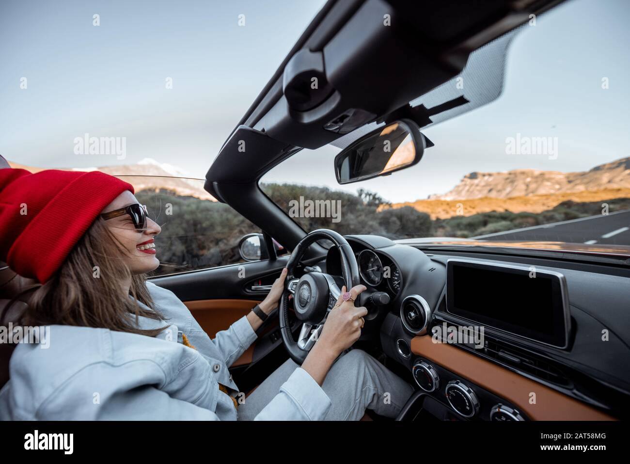 Happy woman in red hat driving convertible car while traveling on the ...
