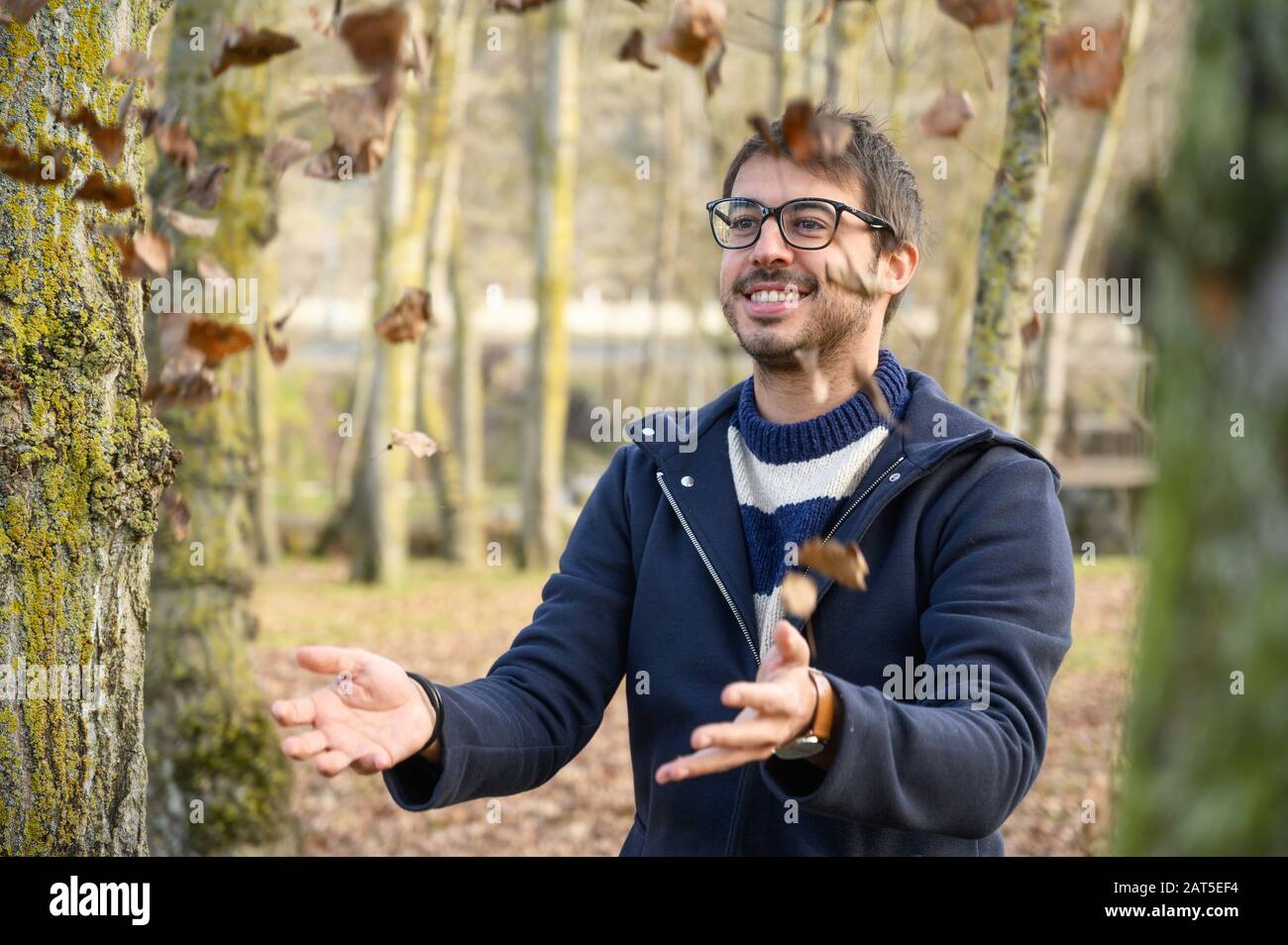 Happy young man playful throwing leaves with open arms dancing under a ...