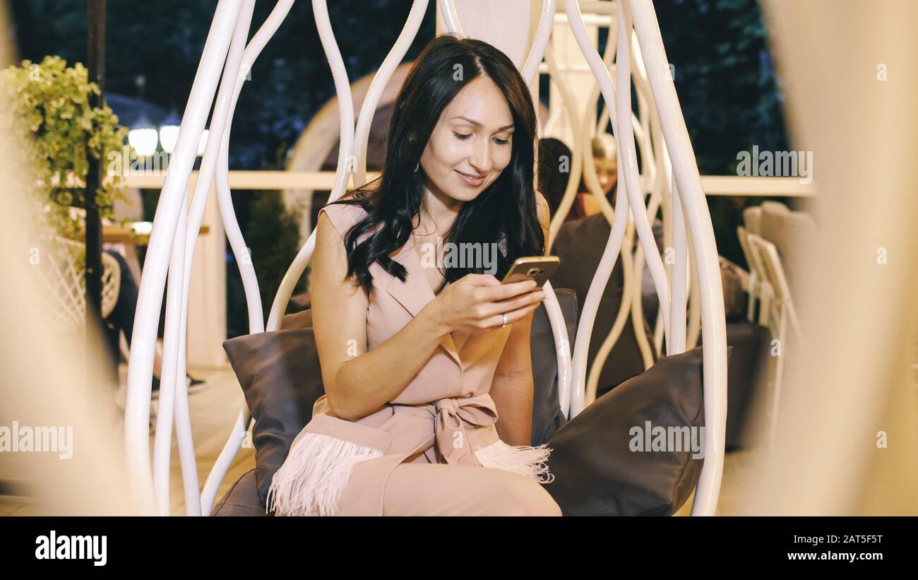 Young beautiful girl browsing smartphone sitting at the bar. She is ...
