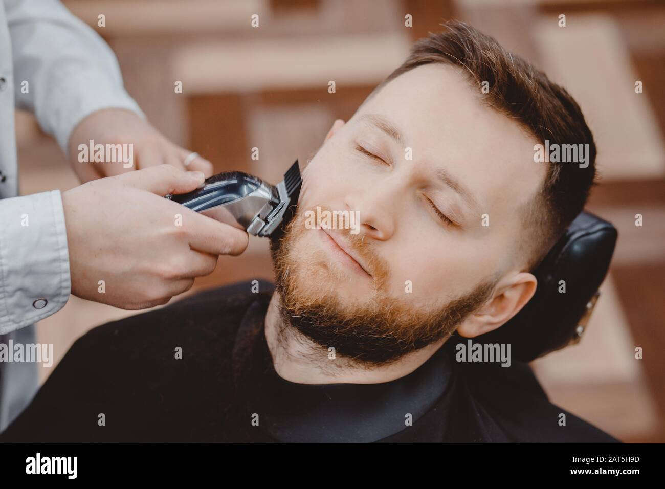 Close-up of barber shearing beard to man in barbershop electric razor ...