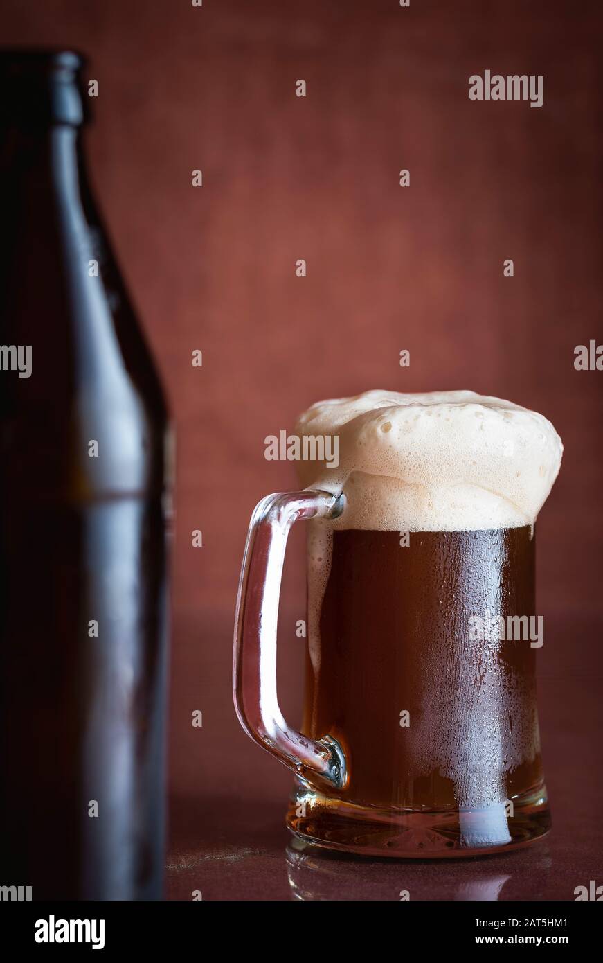 Pint of black beer with foam and frost, on brown background. Cold glass ...