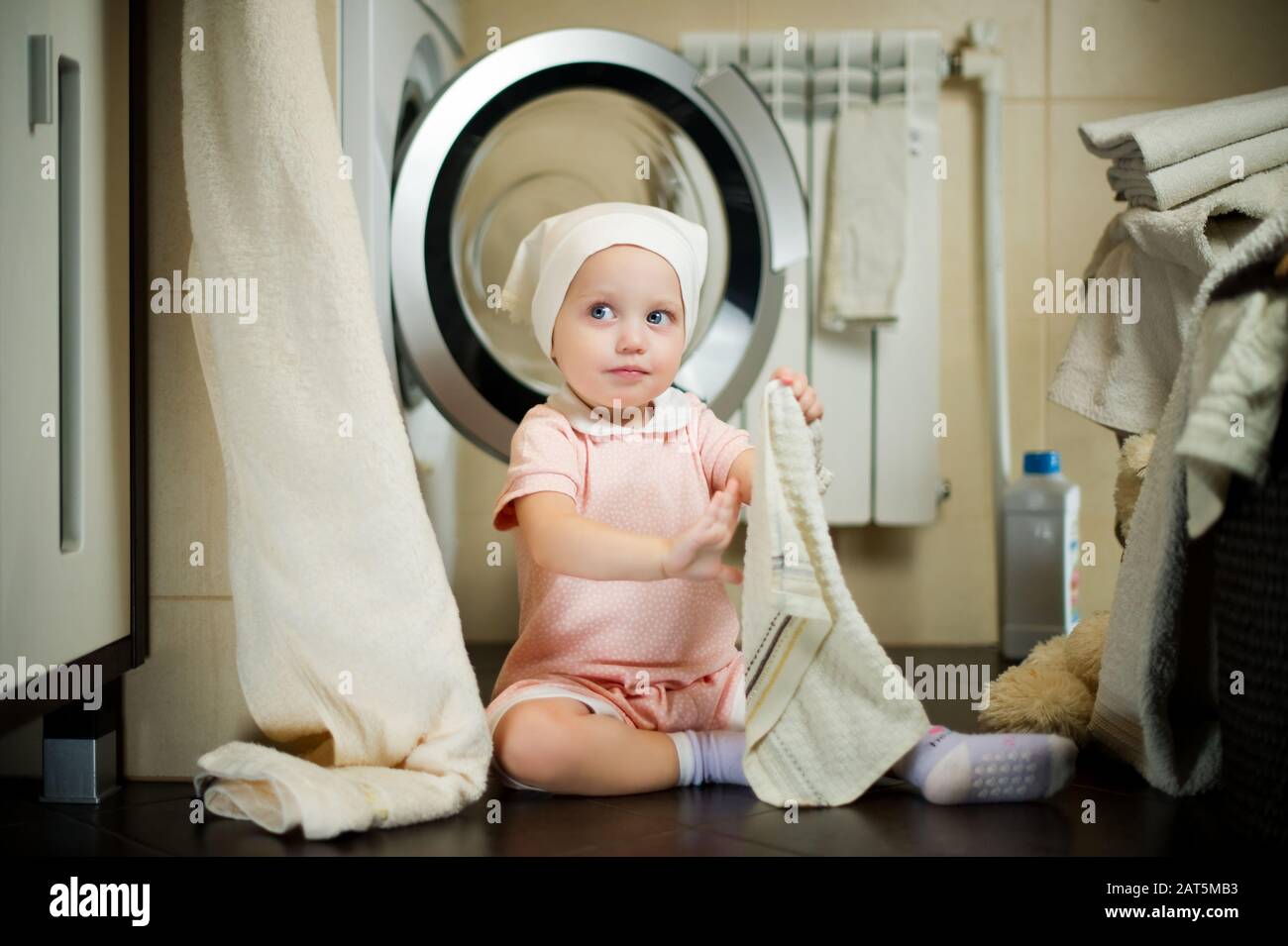 little blue-eyed girl sitting near the washing machine. Baby and ...