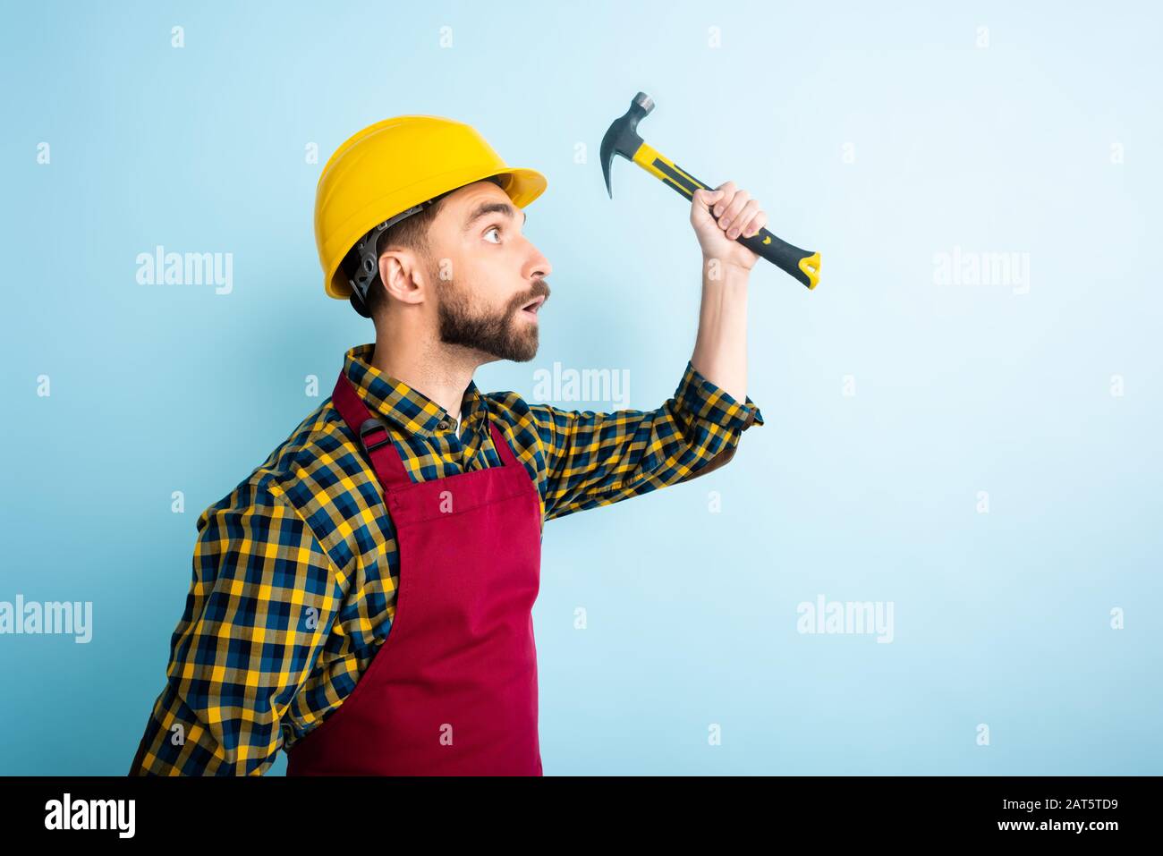 side view of surprised workman holding hummer isolated on blue Stock ...