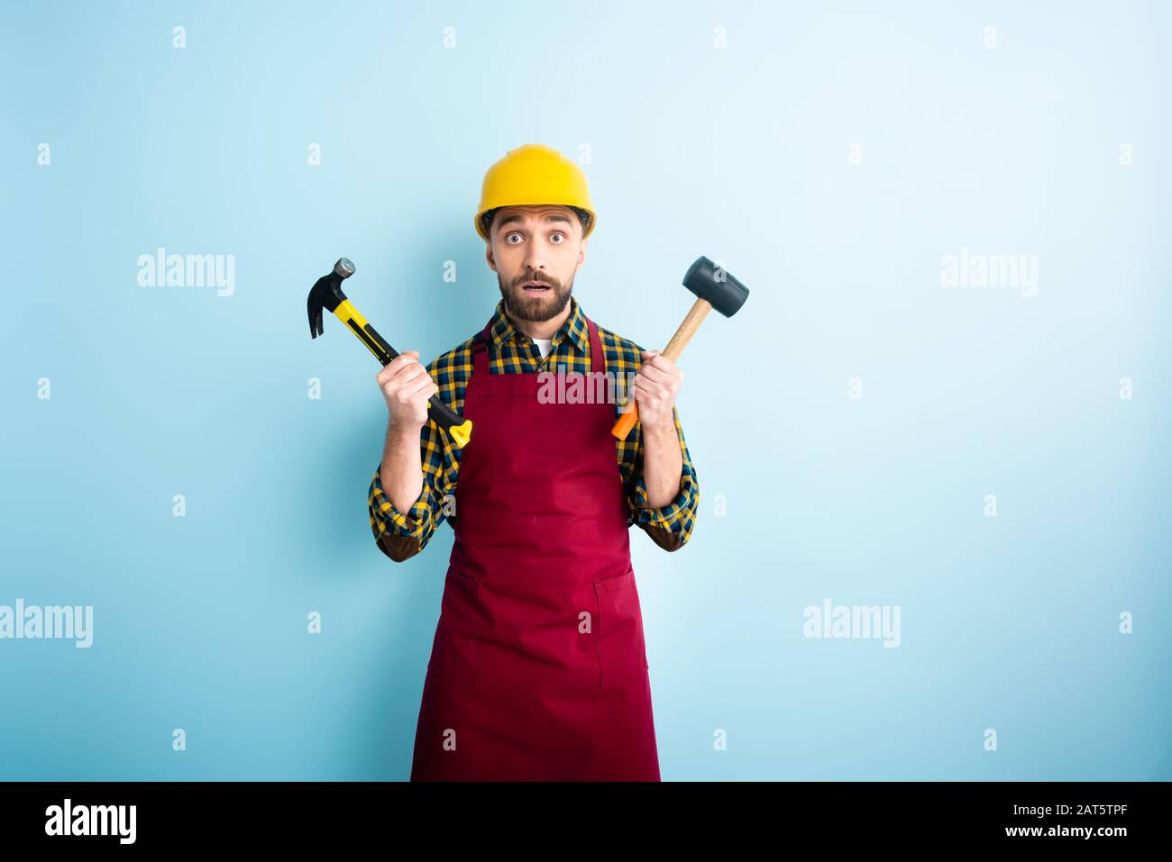 confused workman holding hammers on blue Stock Photo - Alamy