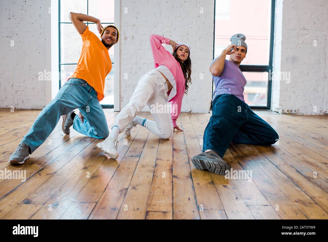 stylish multicultural men in hats breakdancing with beautiful young ...