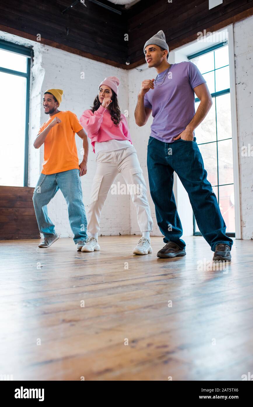 handsome multicultural men in hats breakdancing with attractive girl ...