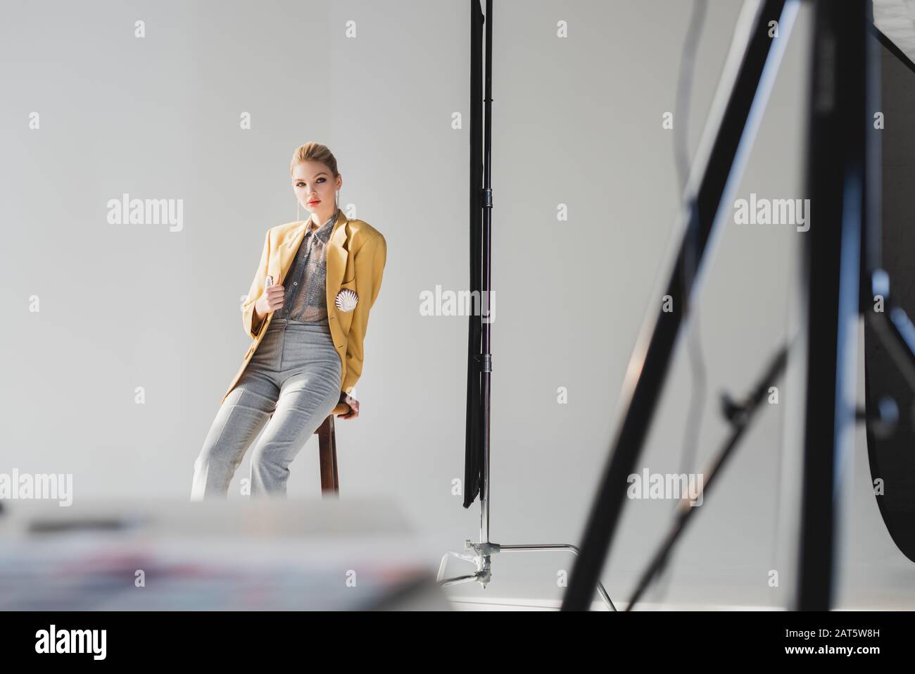 selective focus of stylish model posing and sitting on stool on ...