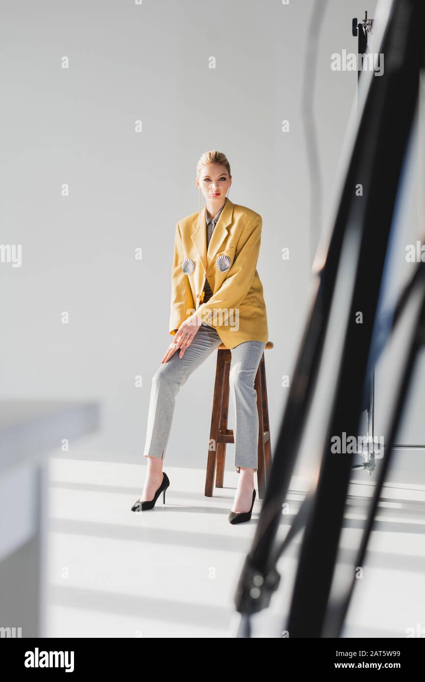 selective focus of stylish model posing and sitting on stool on ...