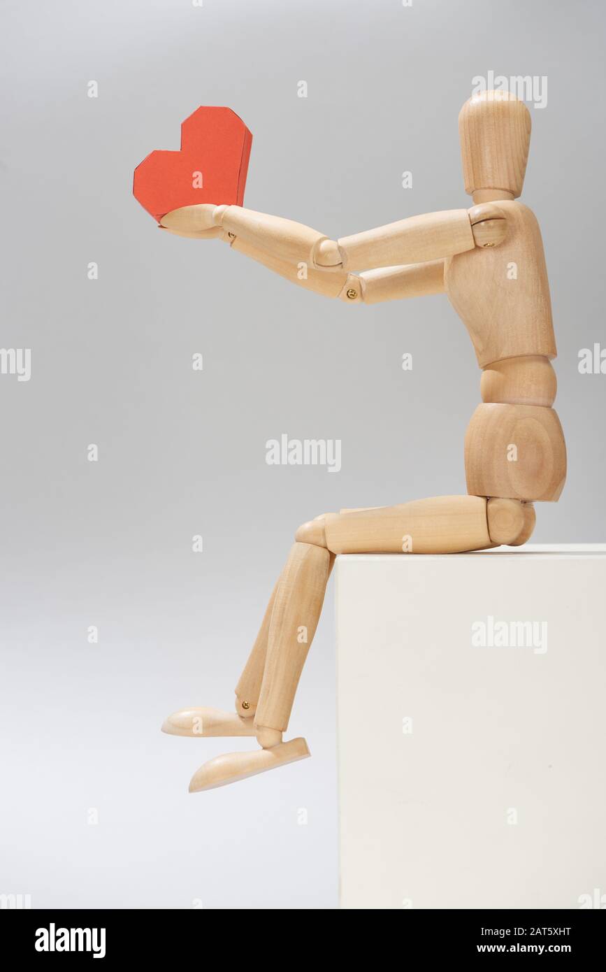 Wooden puppet with paper in heart shape on stand on grey background ...