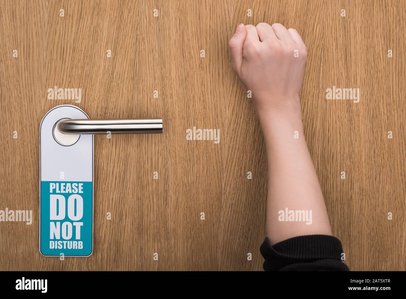 cropped view of woman knocking at door with please do no disturb sign ...