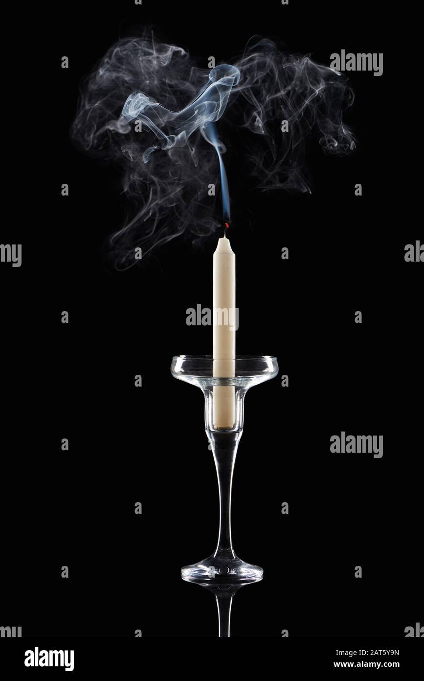 extinct white candle in glass candlestick with smoke on black ...