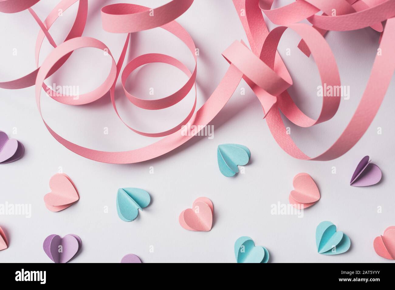 top view of small paper hearts and pink paper swirl on white background ...