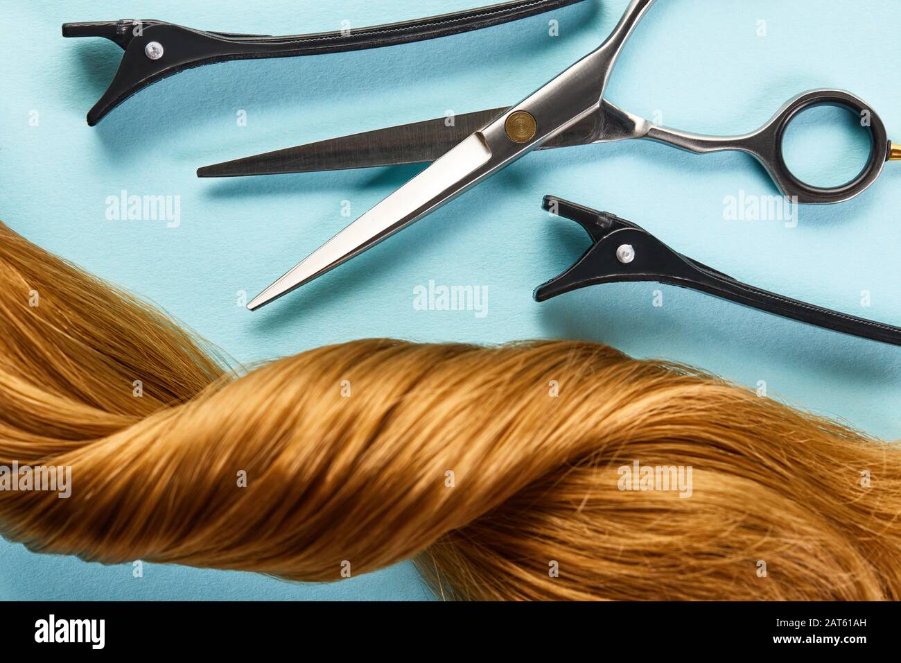 Top view of clamps and scissors with twisted brown hair on blue ...