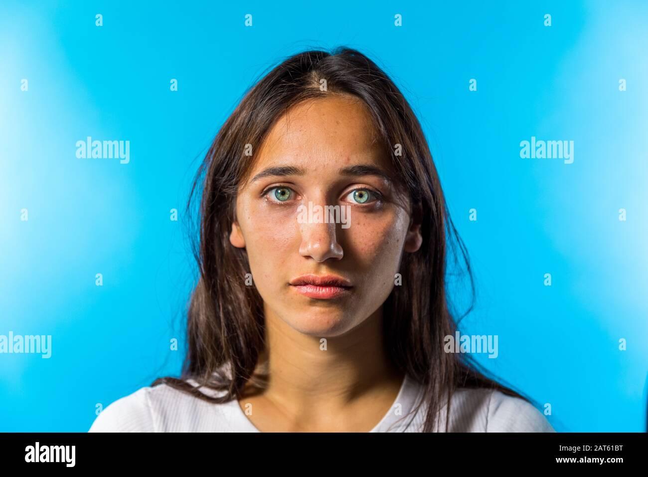 Beauty shot of young woman with light colored eyes on blue background ...