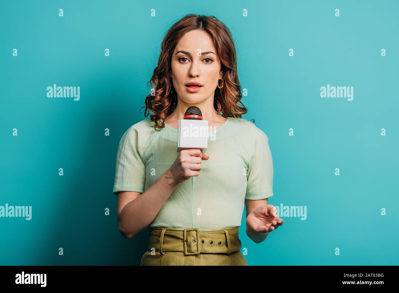 serious journalist looking at camera while holding microphone on blue ...